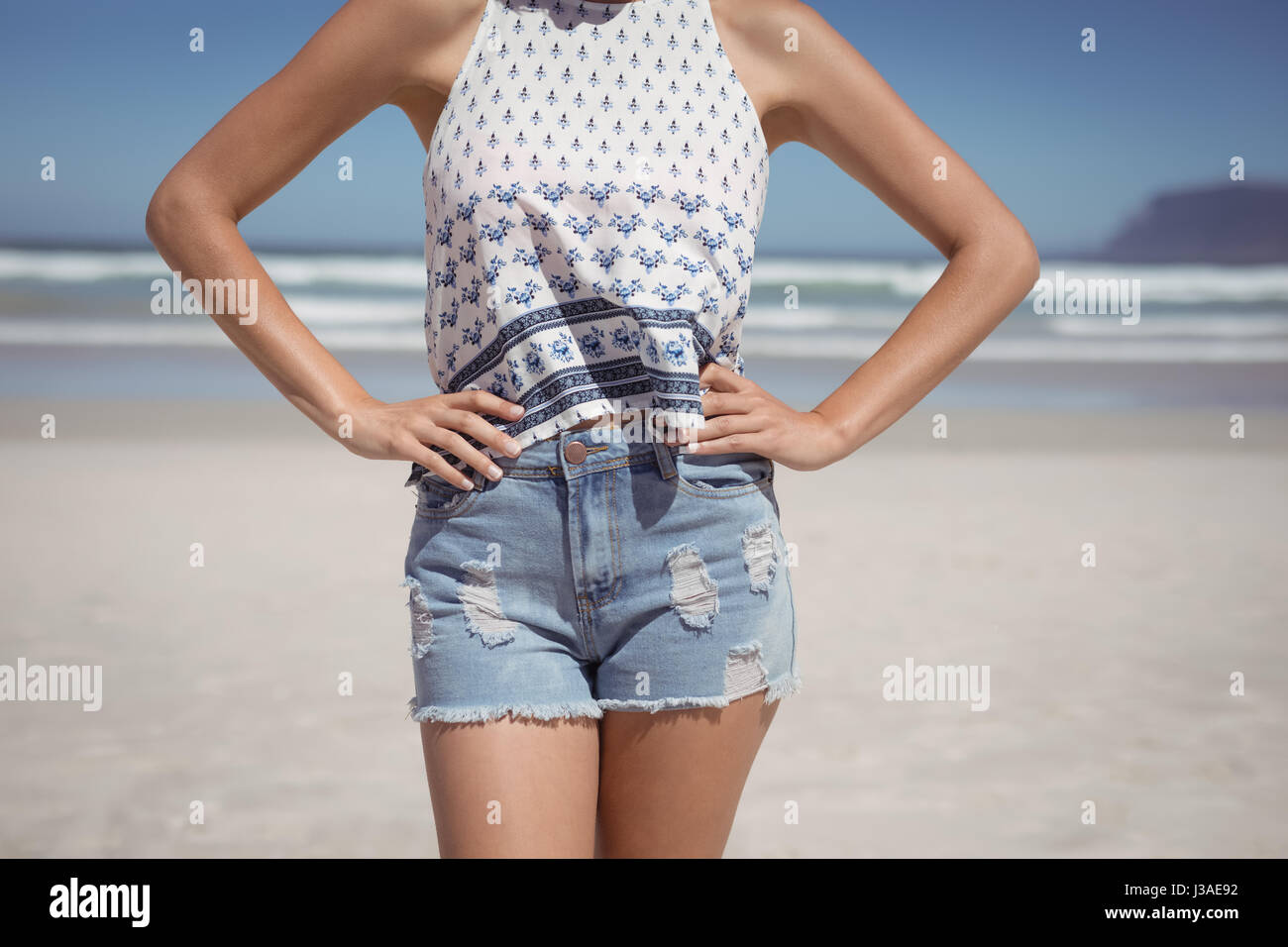 Mid section of woman with hands on hip standing at beach during sunny ...
