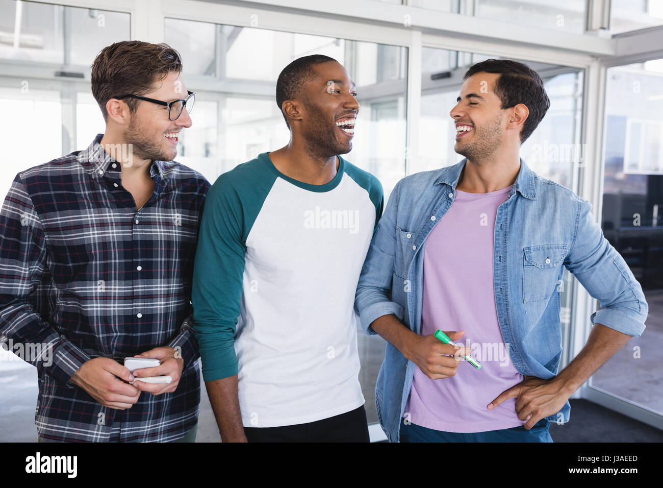 Cheerful male business colleagues standing together at creative office ...