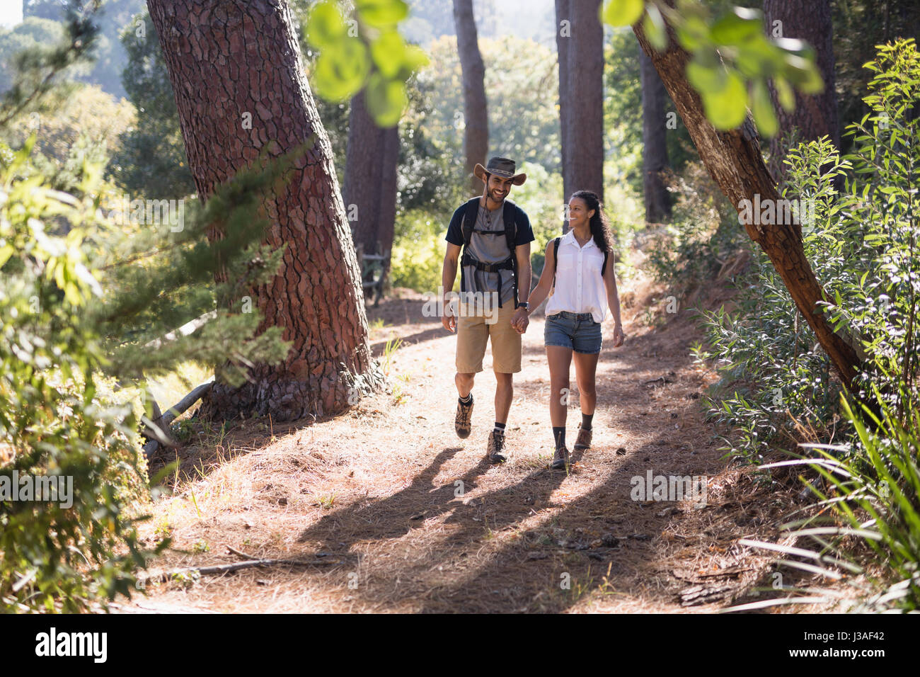 Happy young couple hiking on trail amidst plants in forest Stock Photo ...