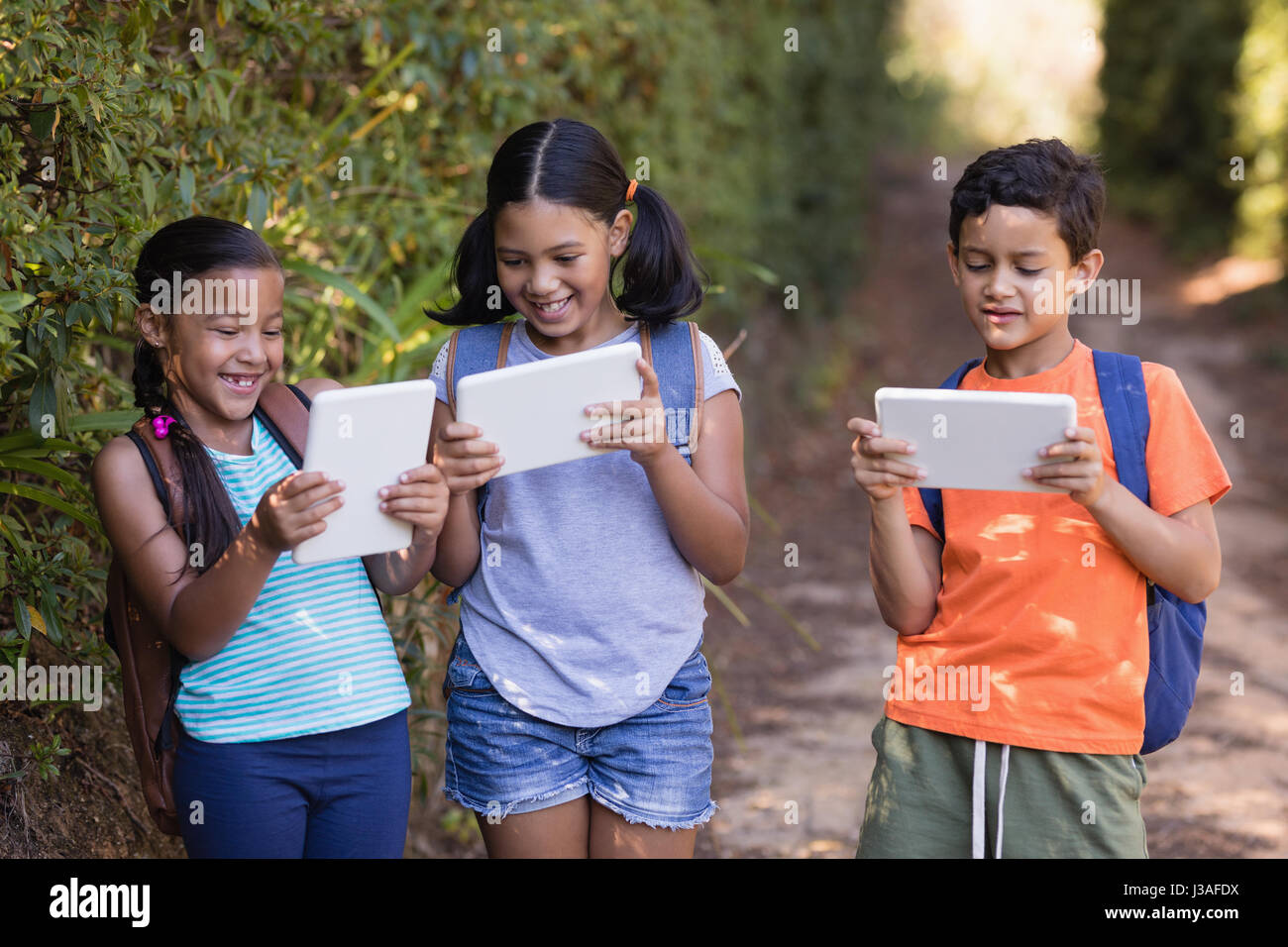 Smiling friend using digital tablets while walking at natural parkland ...