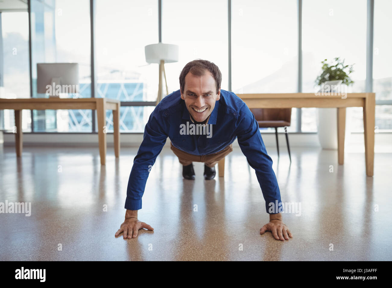 Portrait of smiling executive doing push-ups in office Stock Photo - Alamy
