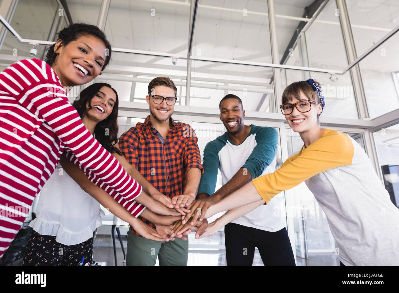 Portrait of smiling business people stacking hands while standing in ...