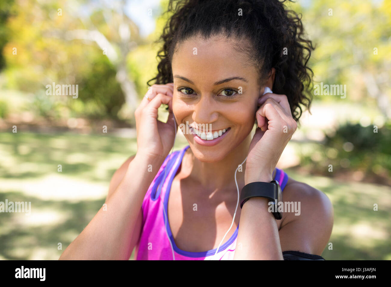 Close-up of smiling jogger woman adjusting her headphones in the park ...