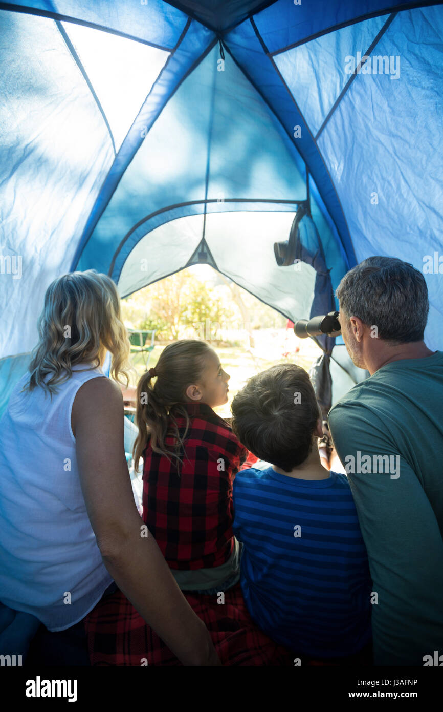 Rear view of family looking through telescope while sitting in the tent ...