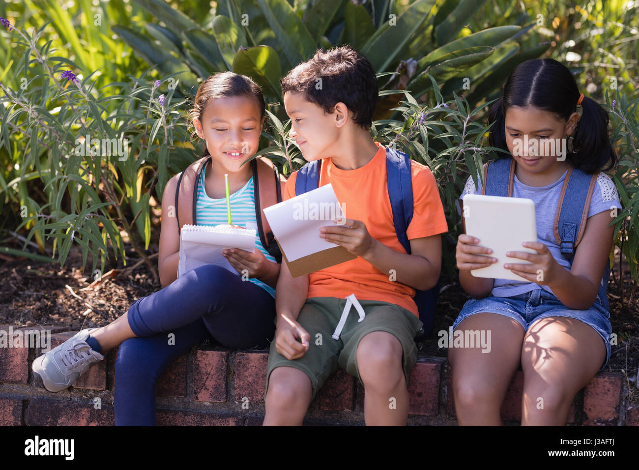 Little girl using digital tablet while friends discussing over book at ...
