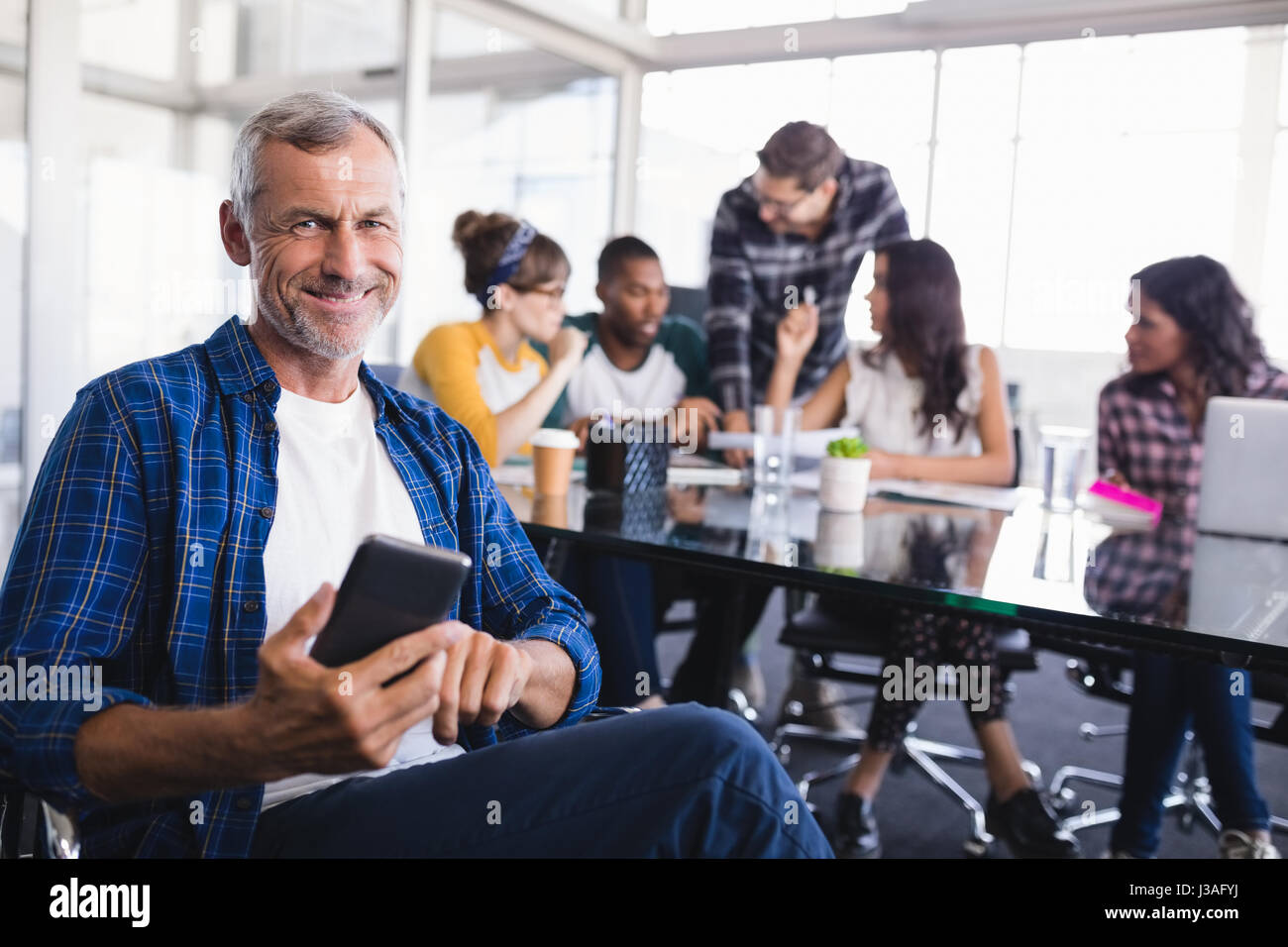 Portrait of happy businessman using mobile phone with team working in ...