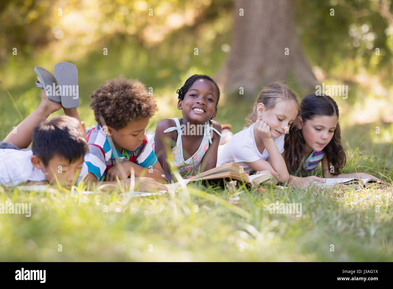 Friends reading book while lying on grassy field at campsite Stock ...