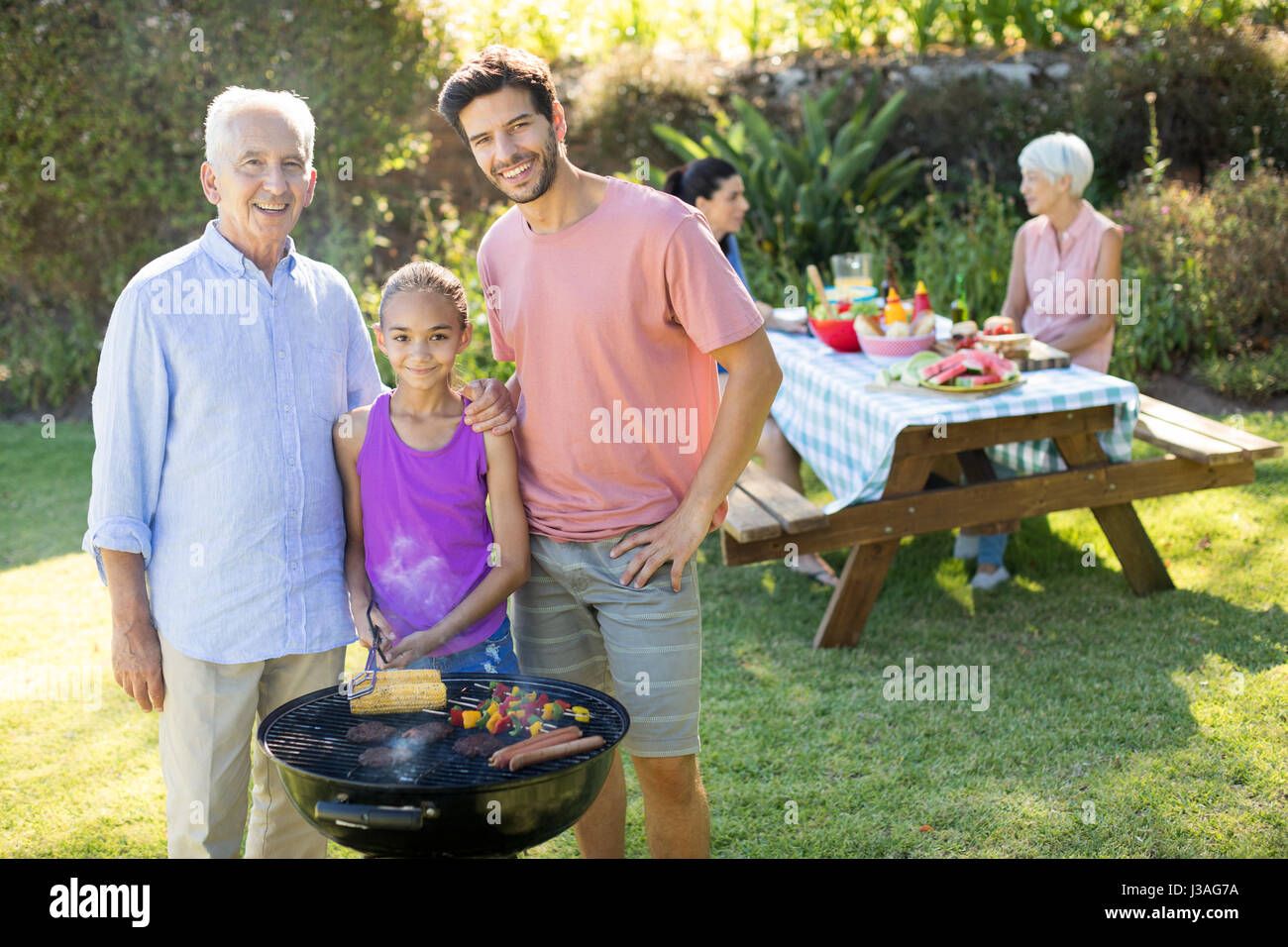 Portrait of girl, father and grandfather preparing barbecue in the park ...