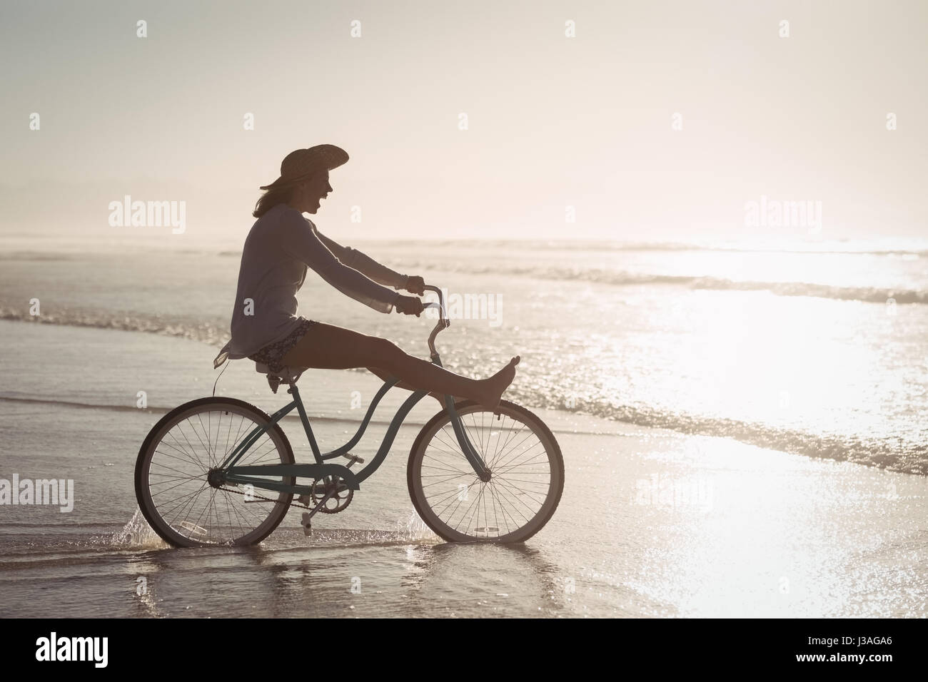 Side view of cheerful woman riding bicycle on shore at beach during ...