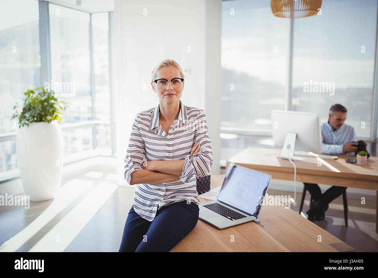 Portrait of confident executive sitting with arms crossed on desk in ...