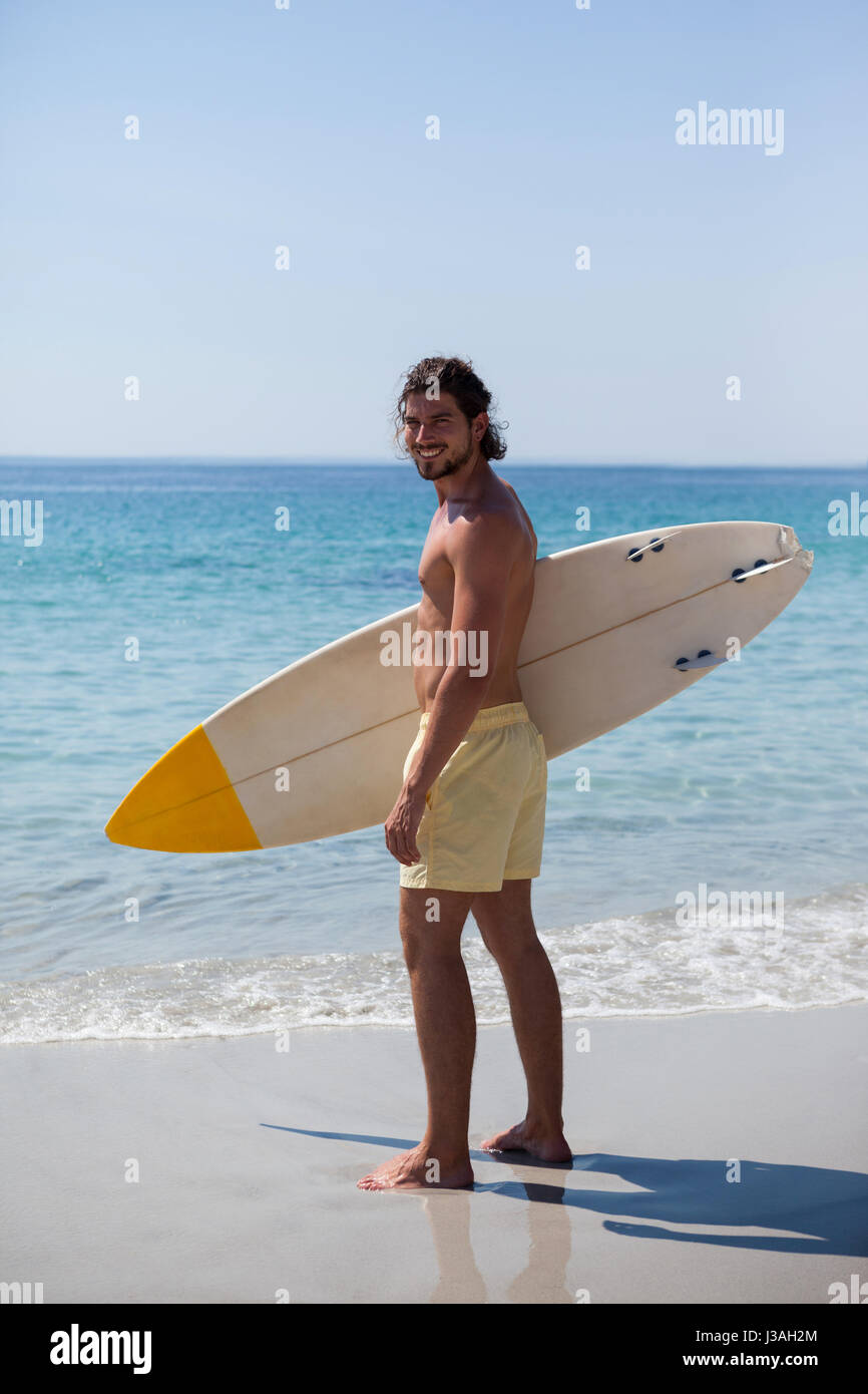 Portrait of smiling surfer with surfboard standing at beach coast Stock ...