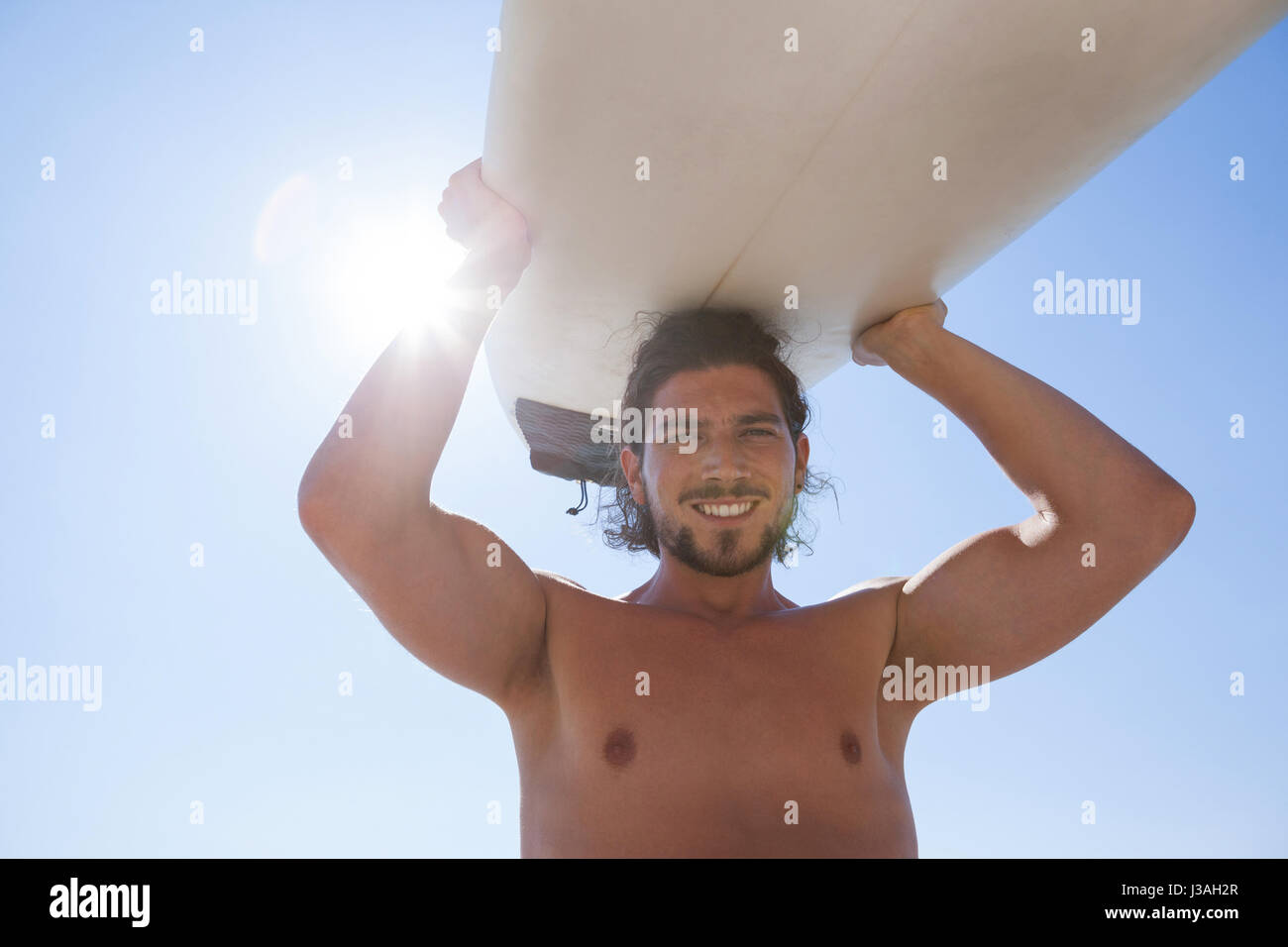 Portrait of surfer carrying surfboard over head at beach coast against ...