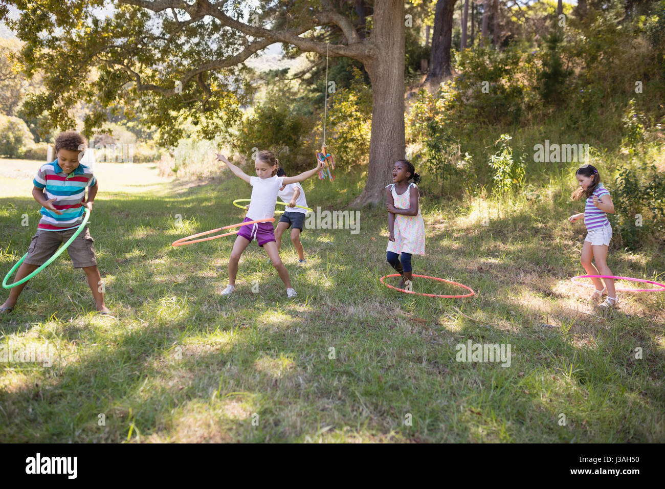 Group of friends playing with hula hoops on grassy field at campsite ...