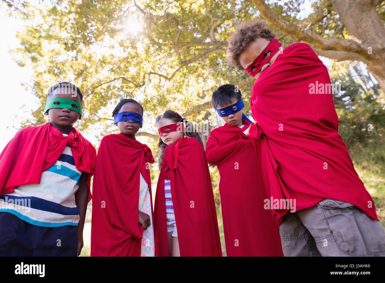 Low angle view of friends in superhero costumes standing at campsite ...