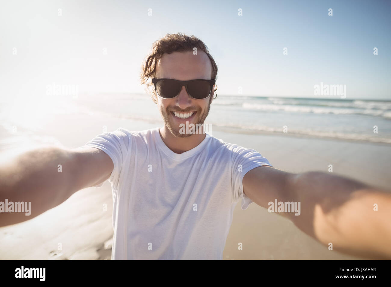 Portrait of smiling young man wearing sunglasses at beach during sunny ...