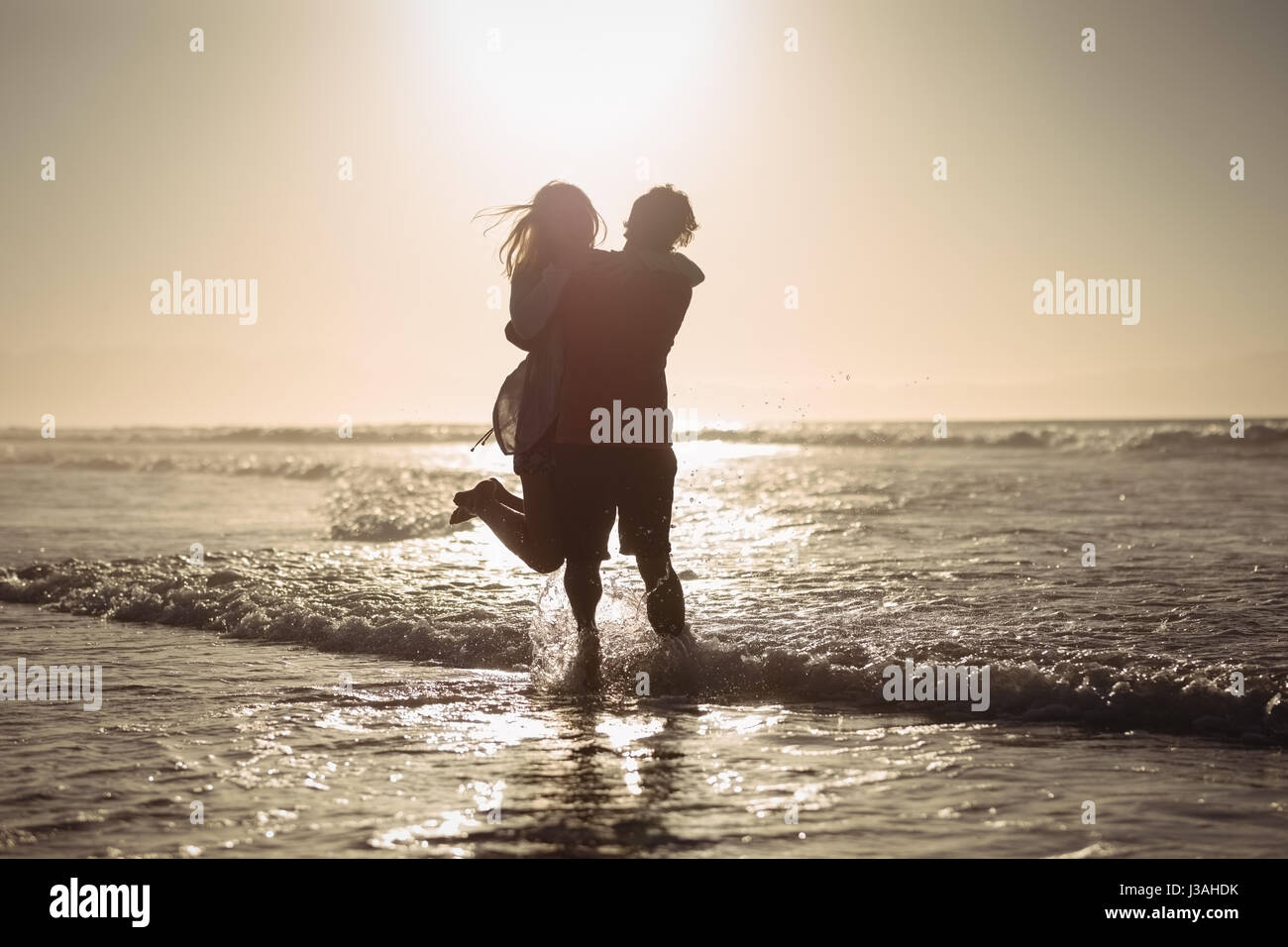 Silhouette couple enjoying on shore at beach during sunny day Stock ...