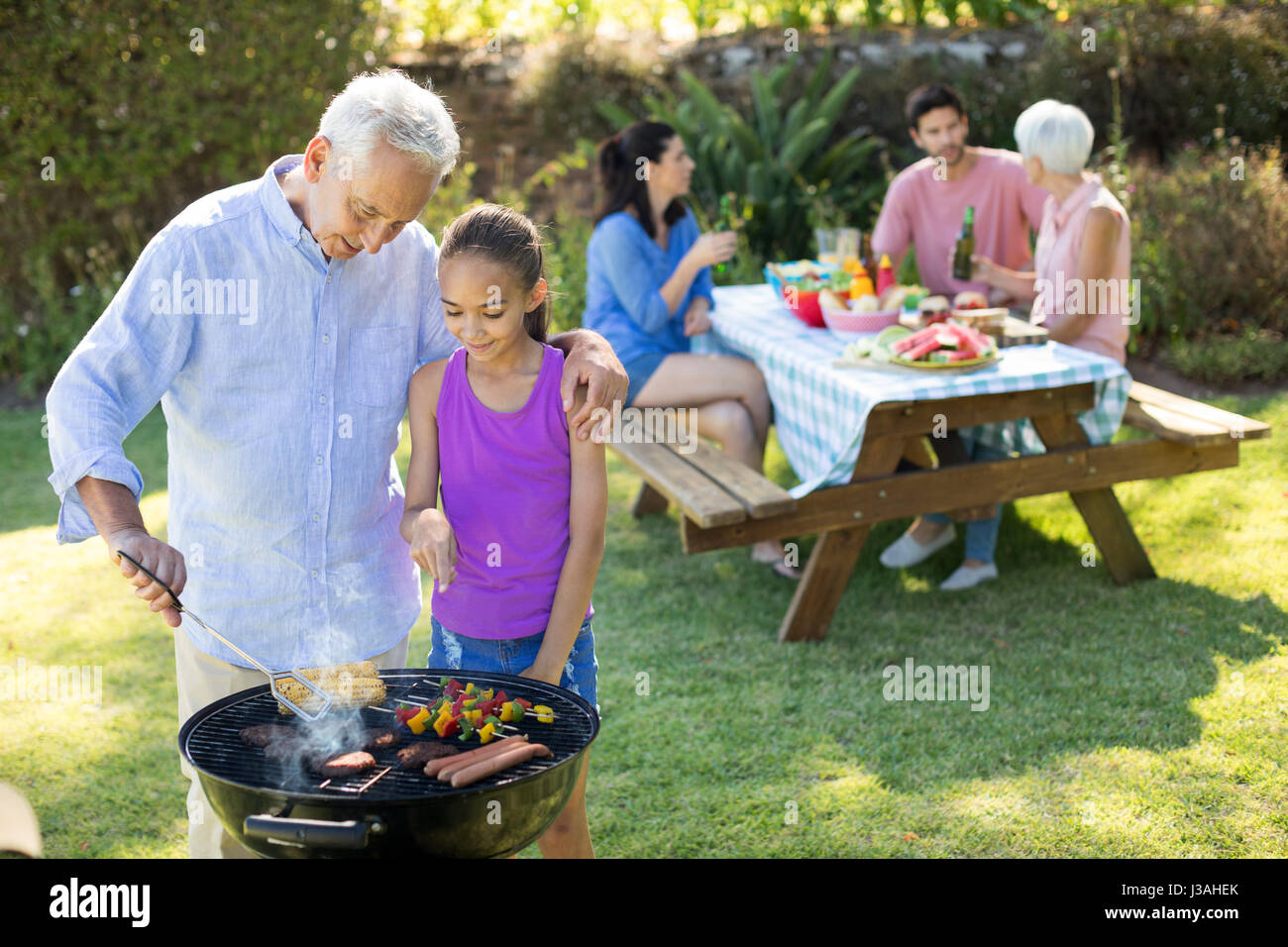 Grandfather and granddaughter preparing barbecue while family having ...