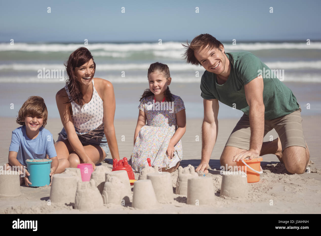 Portrait of happy family making sand castle at beach during sunny day ...