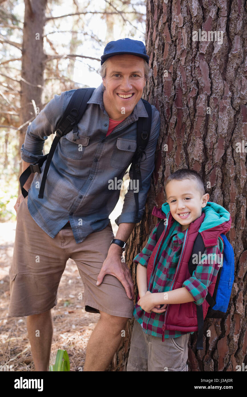 Portrait of happy father and son leaning on tree trunk in forest Stock ...