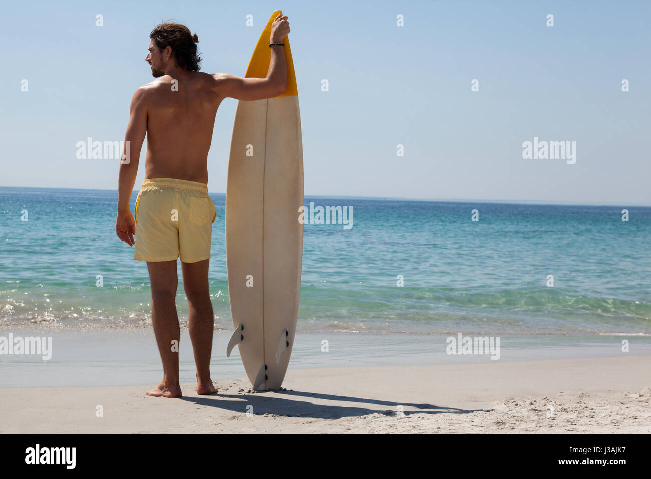 Rear view of surfer with surfboard looking at sea from the beach Stock ...