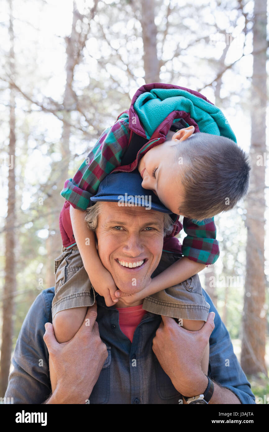 Portrait of happy mature father carrying son on shoulders in forest ...