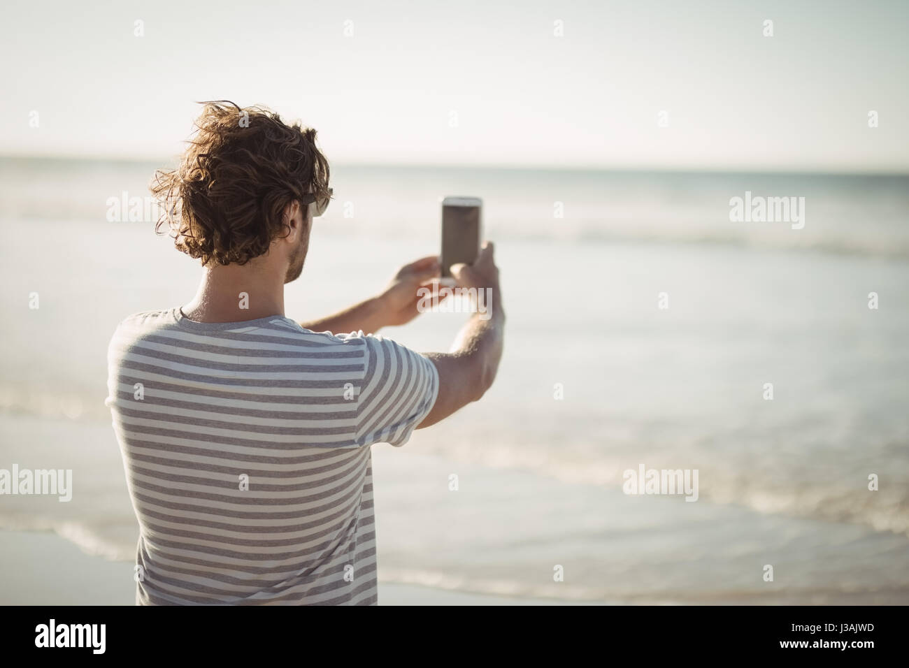 Rear view of man photographing sea at beach during sunny day Stock ...