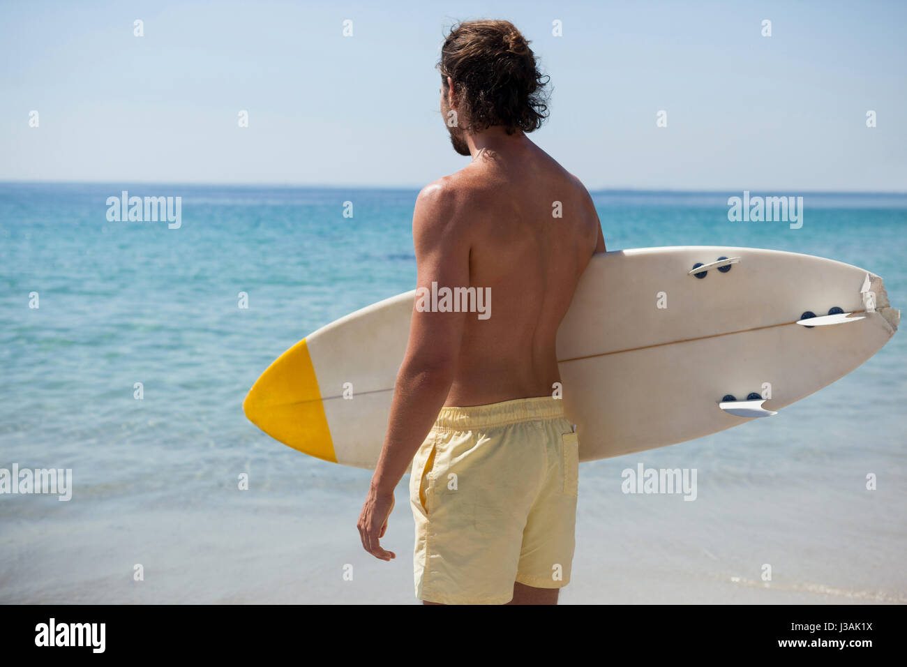Rear view of surfer with surfboard looking at sea from the beach Stock ...