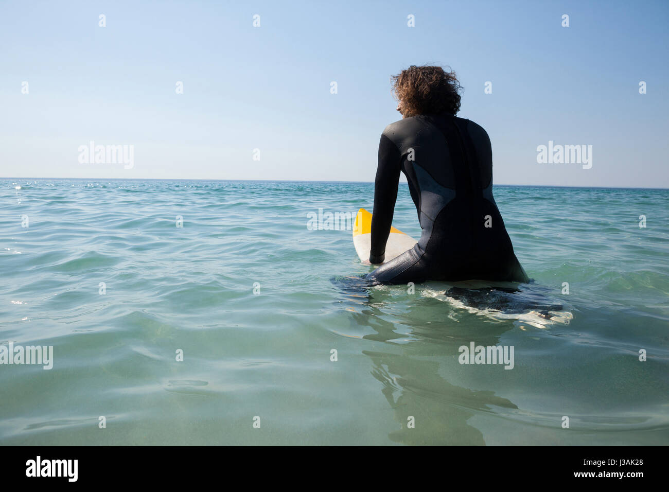 Rear view of surfer sitting on surfboard at seacoast Stock Photo - Alamy