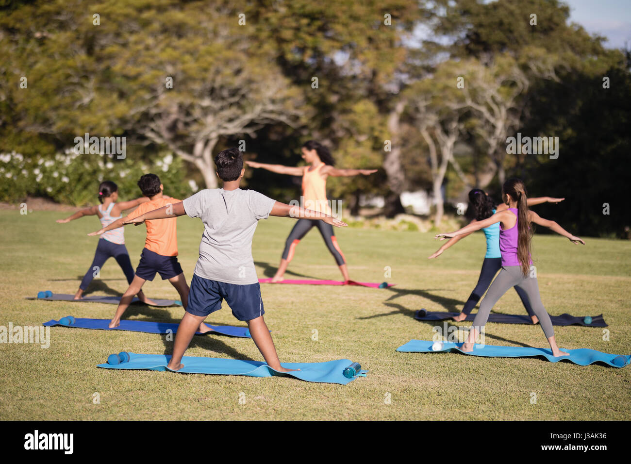 Female trainer teaching children stretching exercise on mat at park ...