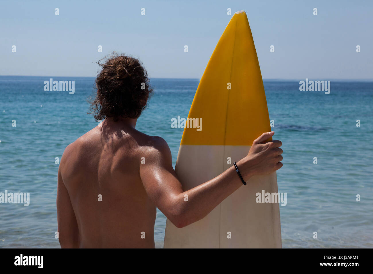 Rear view of surfer with surfboard looking at sea from the beach Stock ...