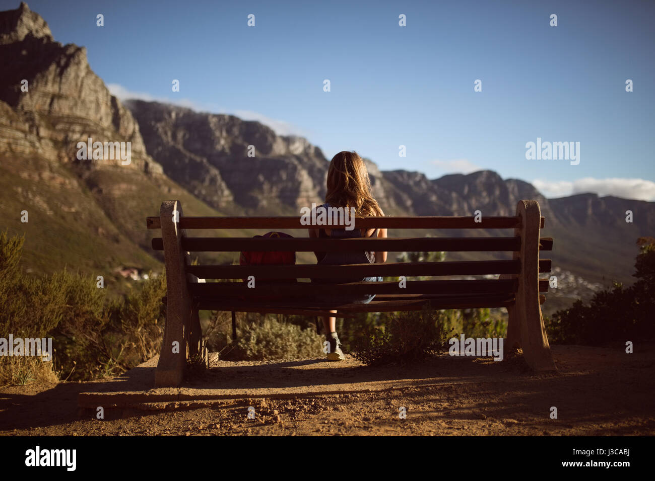 Rear view of woman sitting on bench in countryside Stock Photo - Alamy