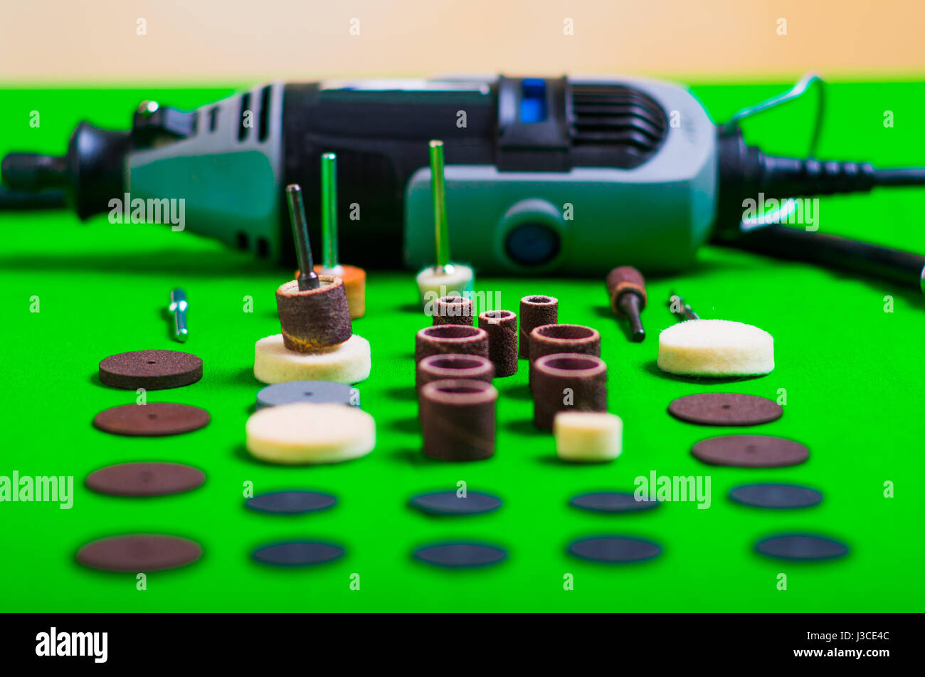 A gray drill behind of the drilling accessories on green background ...
