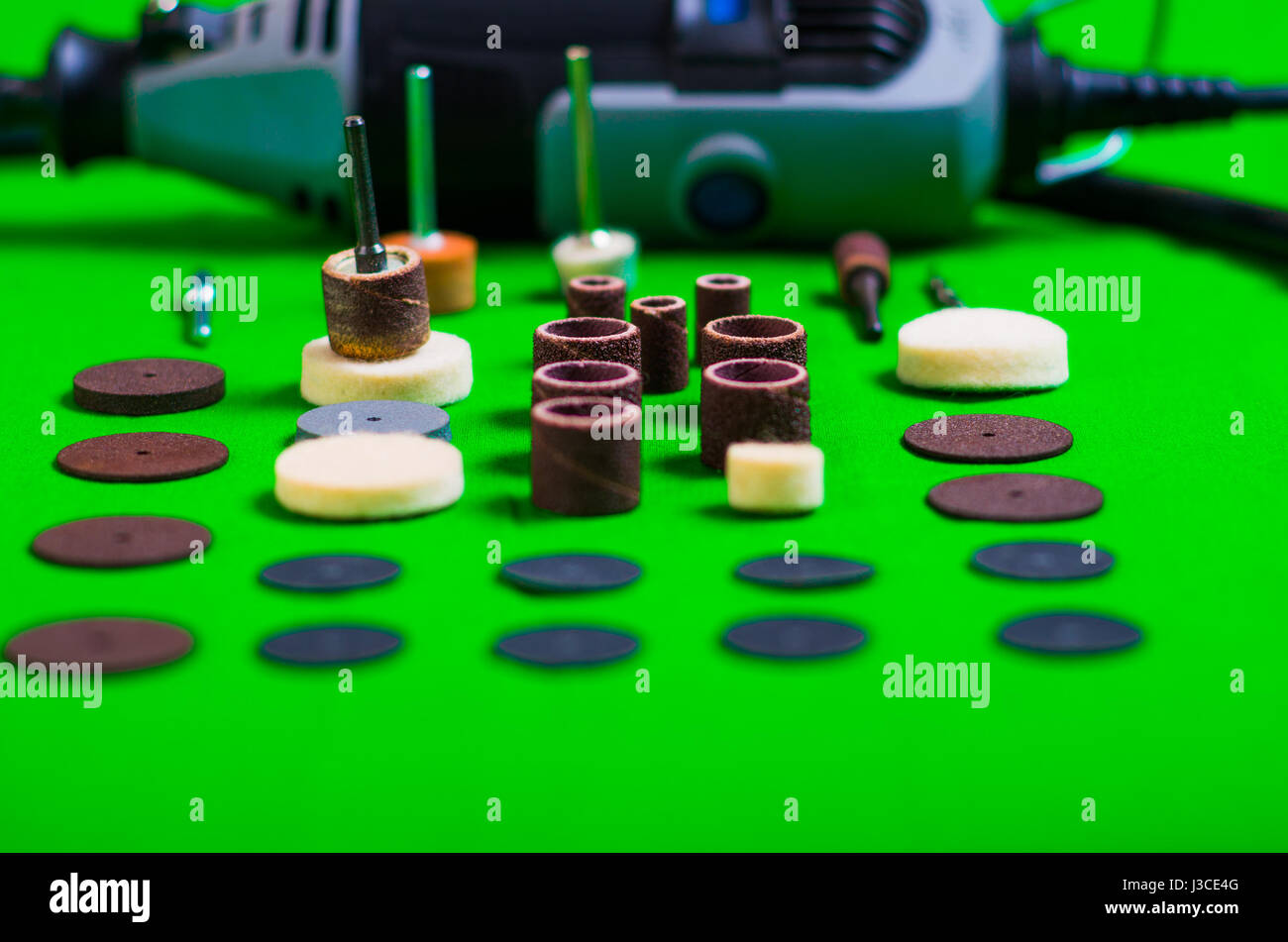 A gray drill behind of the drilling accessories on green background ...