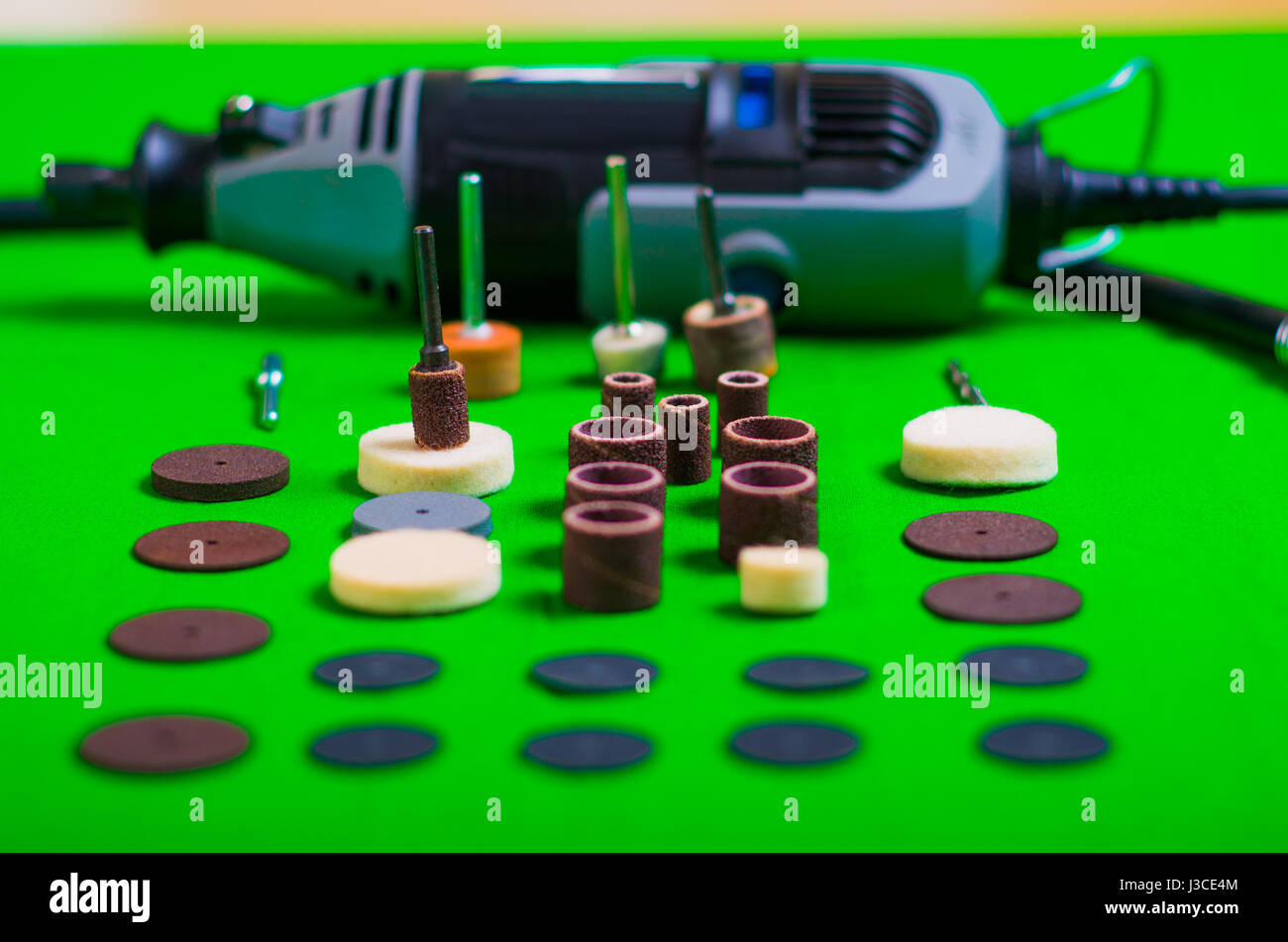 A gray drill behind of the drilling accessories on green background ...