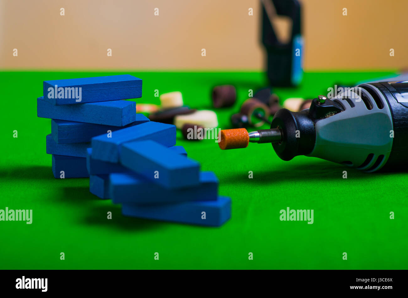 A gray drill with a small blue wooden pieces on a green background ...