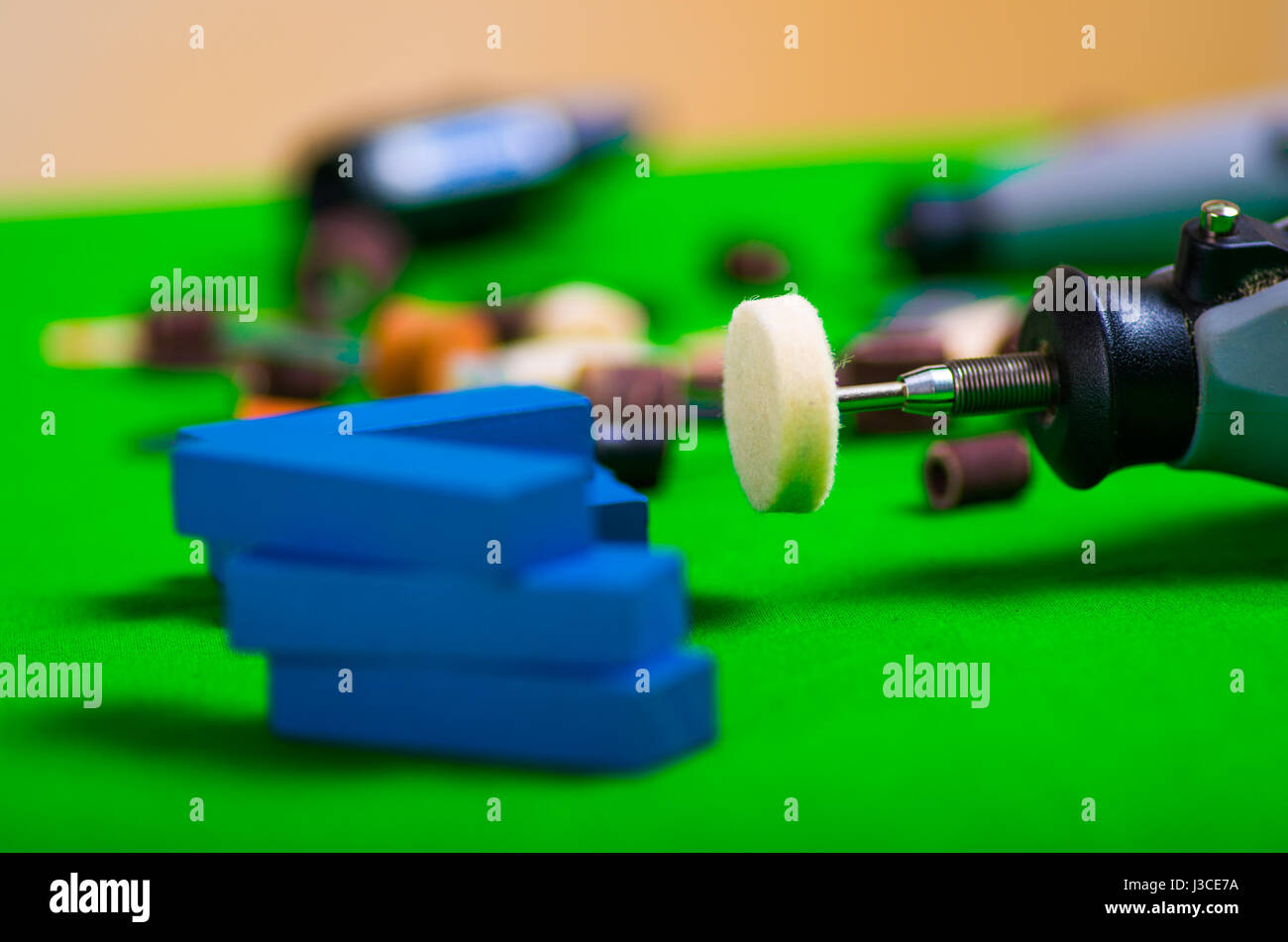 A gray drill with a small blue wooden pieces on a green background ...