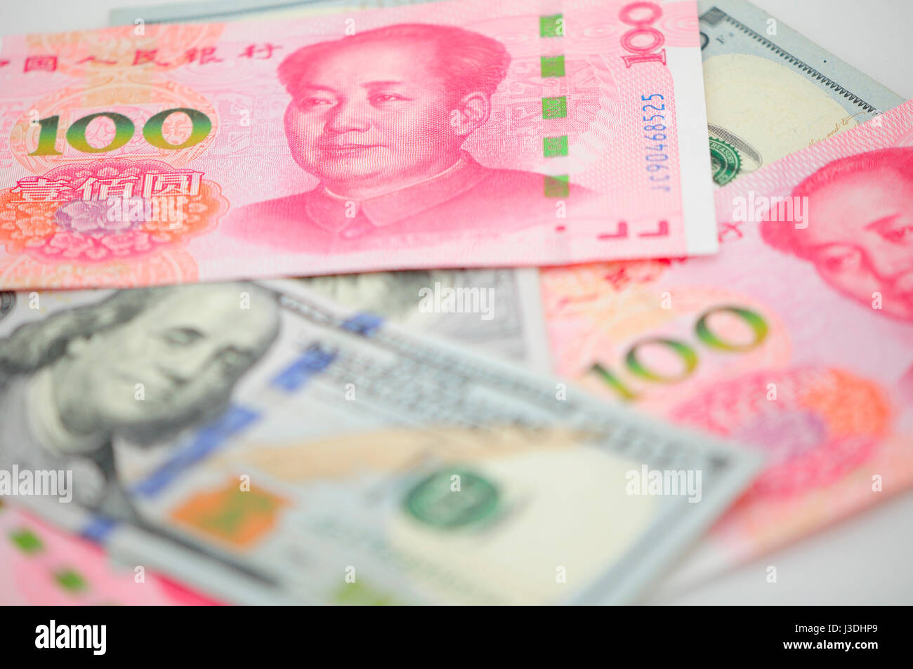 Chinese 100 Renminbi and 100 U.S. dollar bills piled on a white ...