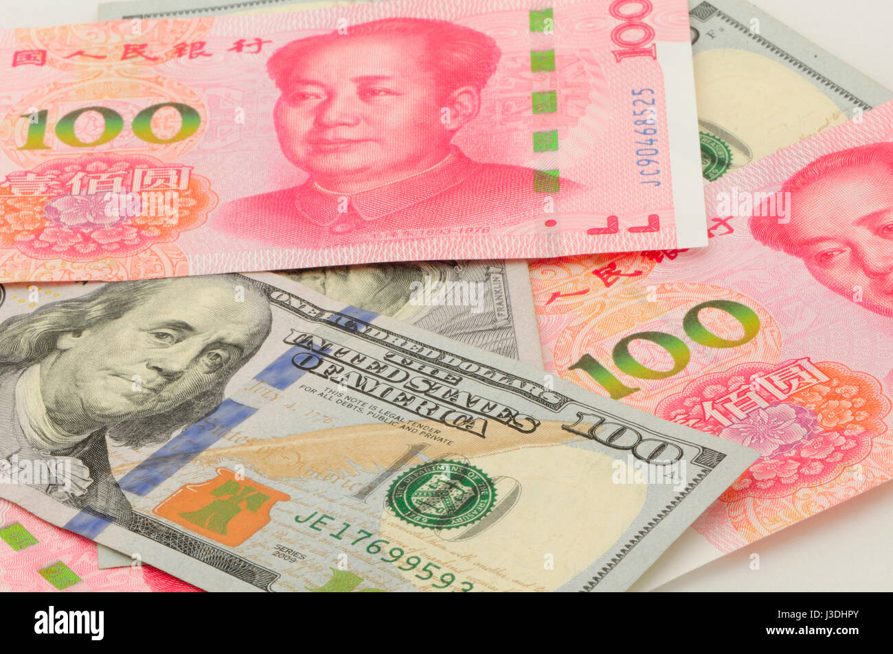 Chinese 100 Renminbi and 100 U.S. dollar bills piled on a white ...