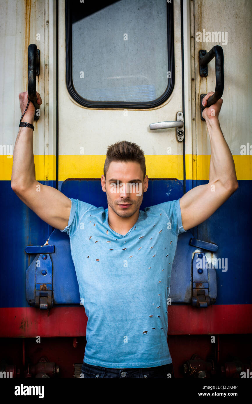 Fit young man hanging from handles outside train Stock Photo - Alamy