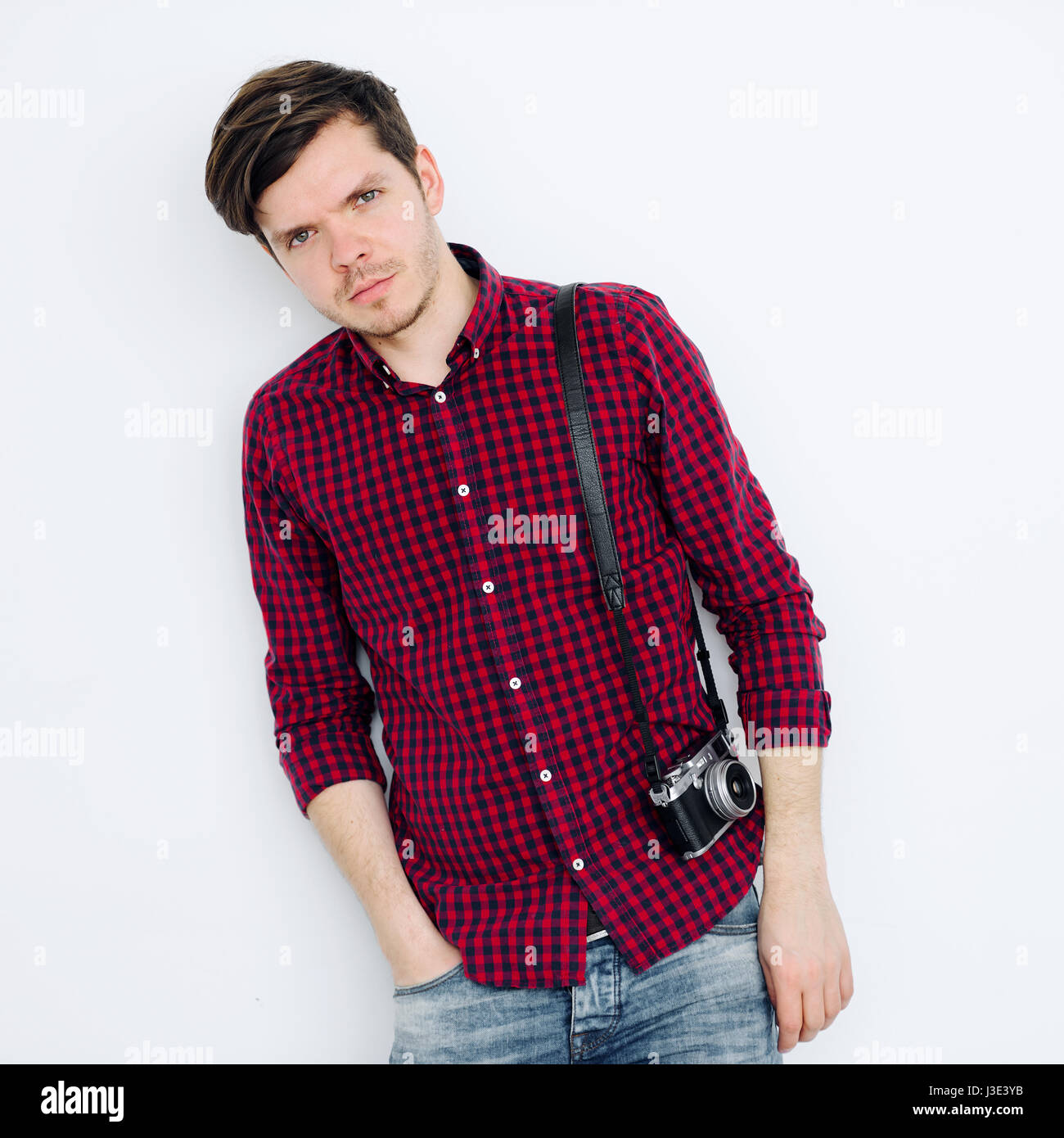 Young and successful man stands near white wall and holds a mirrorless ...