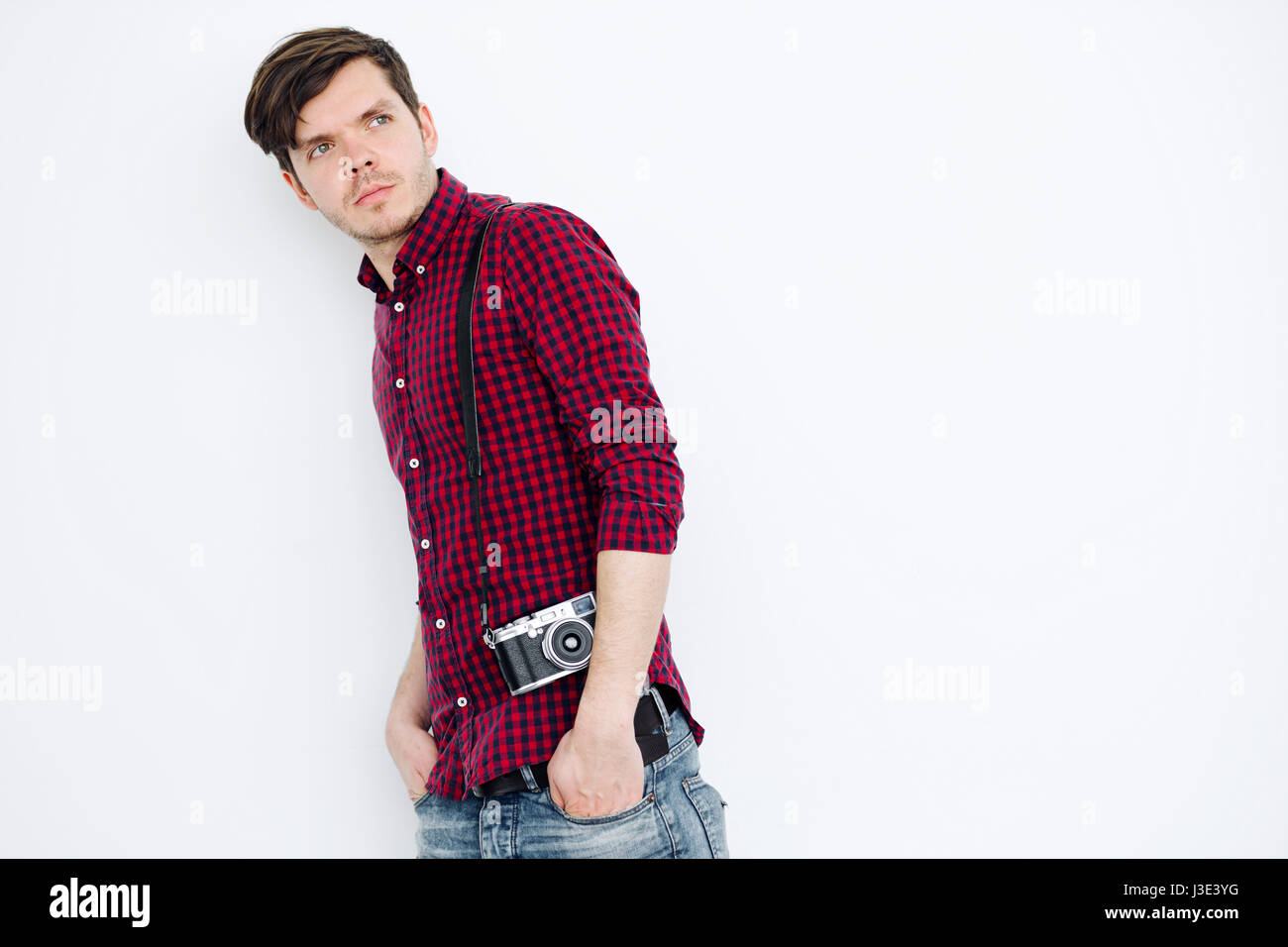 Young and successful man stands near white wall and holds a mirrorless ...