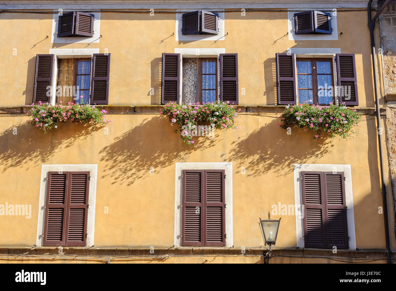 Butter facade with windows, shutters, flower pots and street light ...
