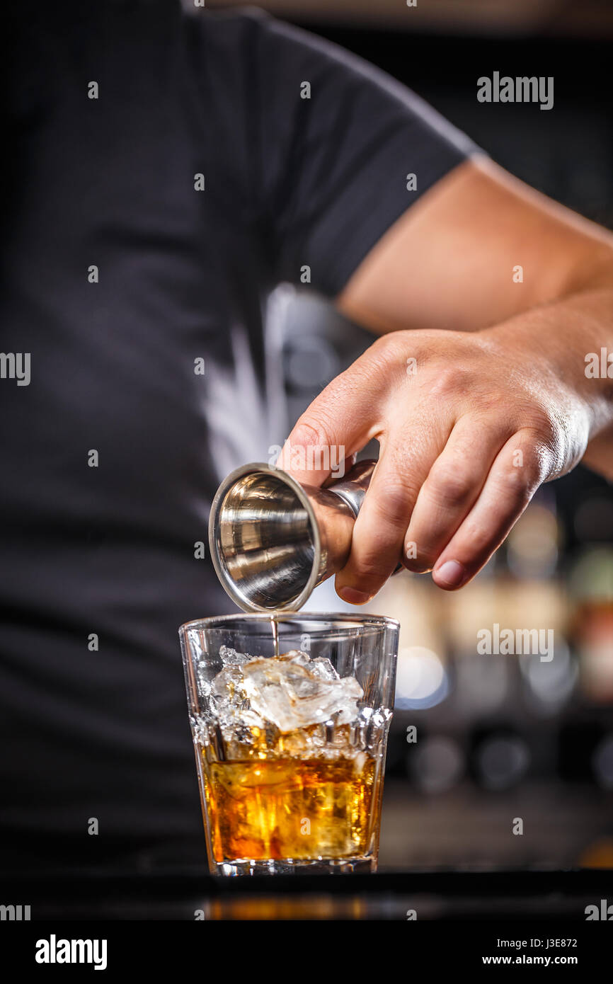 Bartender is pouring alcohol from a measuring glass into a glass over ...