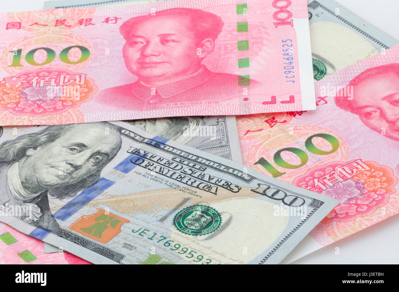Chinese 100 Renminbi and 100 U.S. dollar bills piled on a white ...