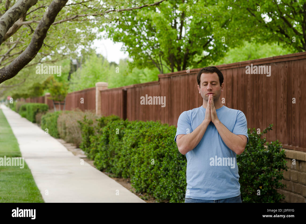 Man praying outside along a pathway and a fence in a neighborhood Stock ...