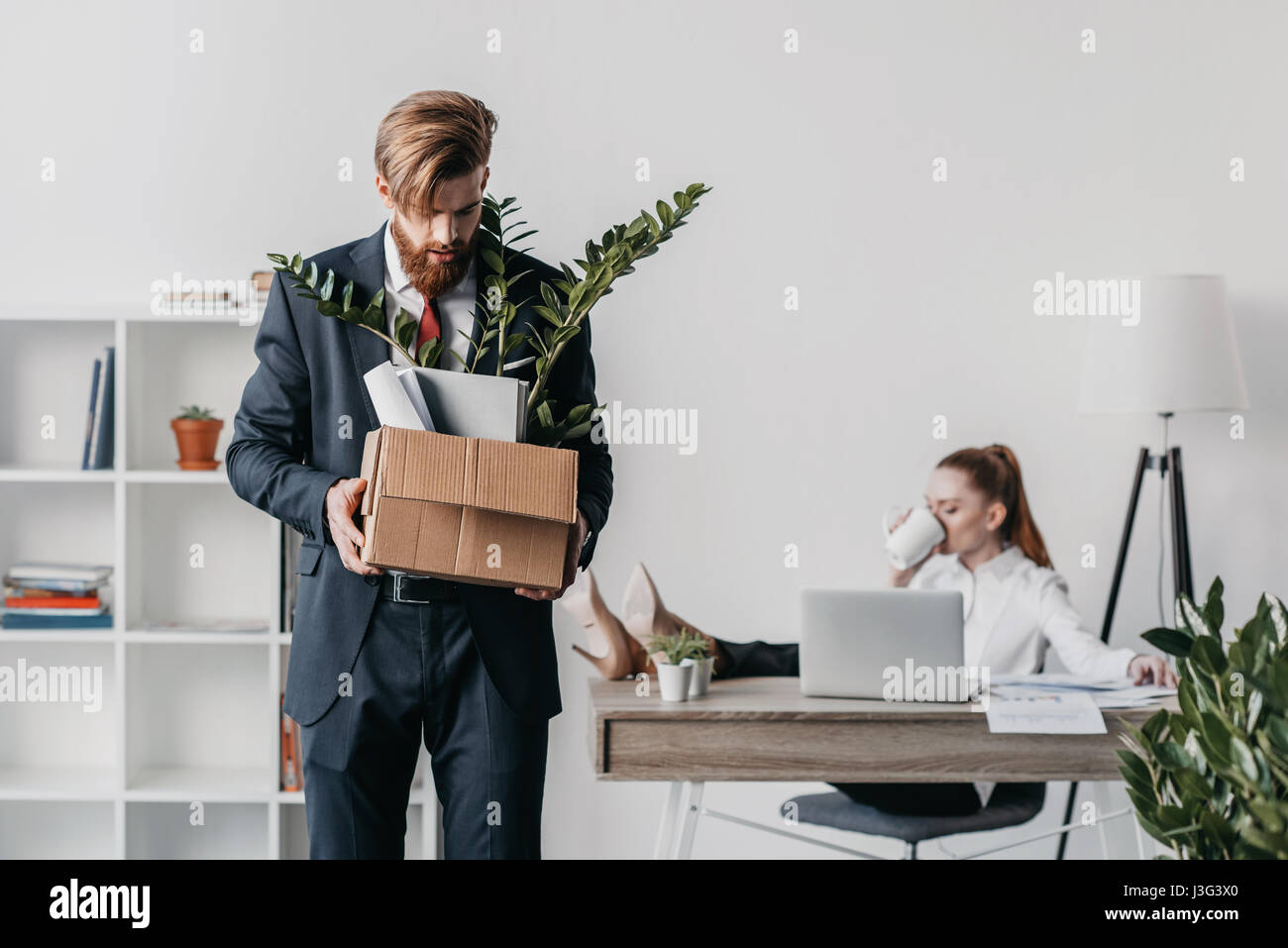 Young upset fired businessman with cardboard box in office, boss behind ...