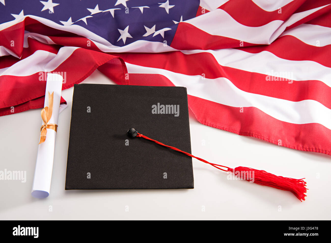 Close-up view of graduation mortarboard, diploma and us flag on white ...