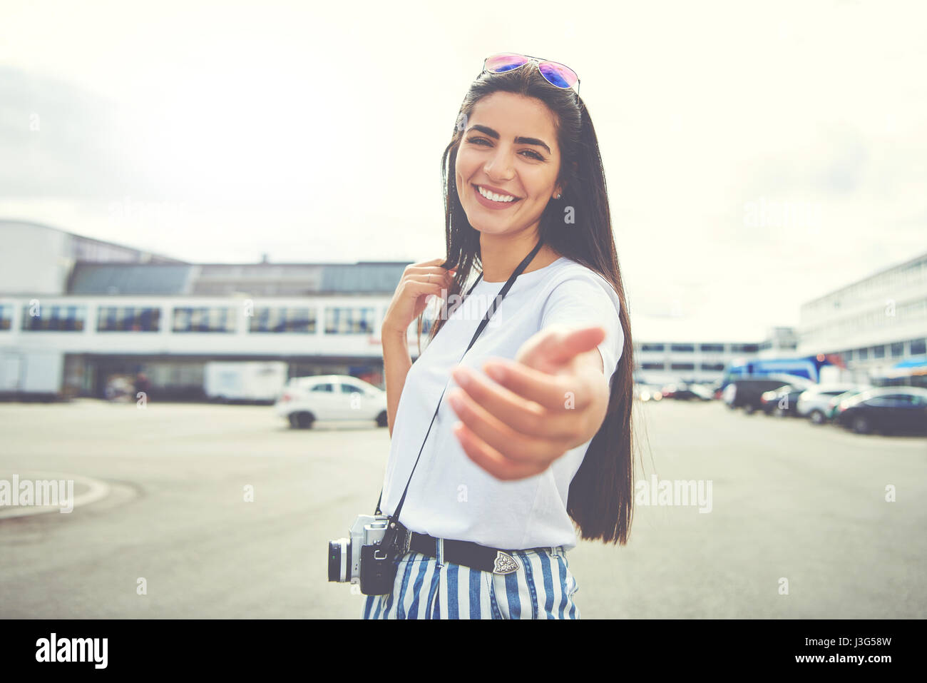 Cute young woman holding out her hand in a gesture of invitation as she ...