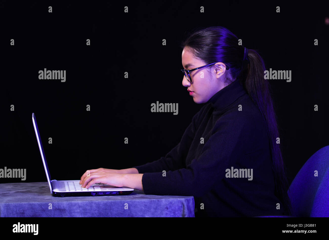 Portrait of a beautiful and smart girl hacker with laptop on dark ...