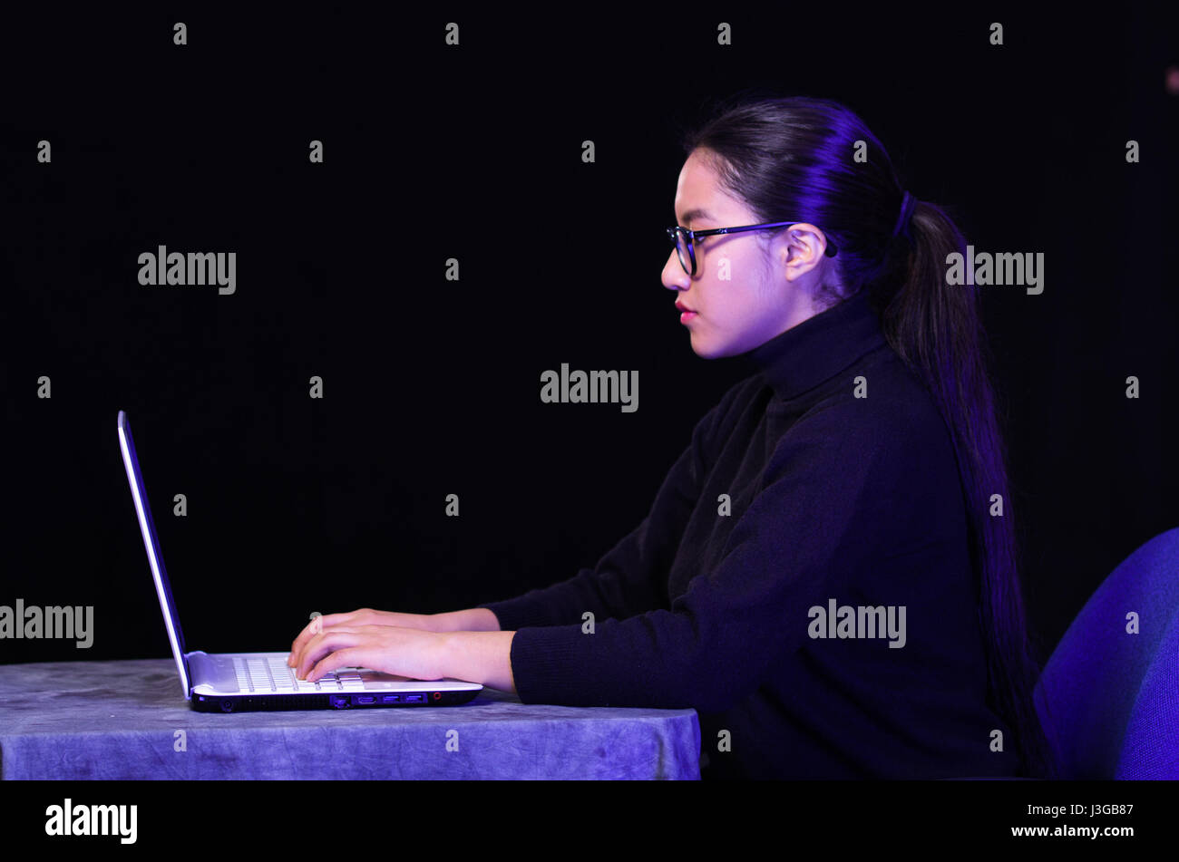 Portrait of a beautiful and smart girl hacker with laptop on dark ...